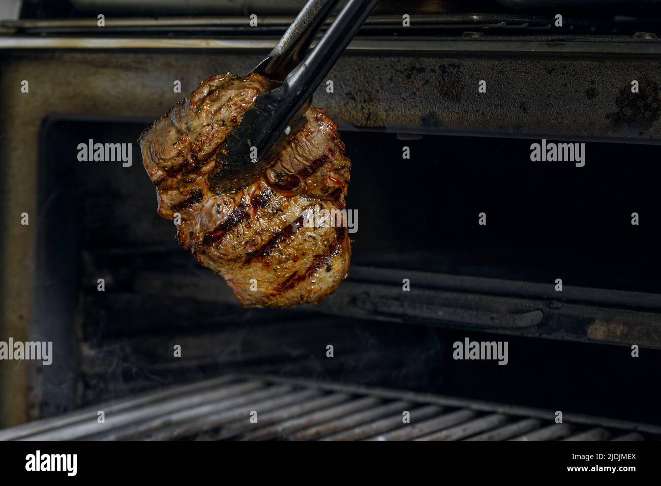 Silver serving kitchen tongs holding meat beef steak grilling on rack ...