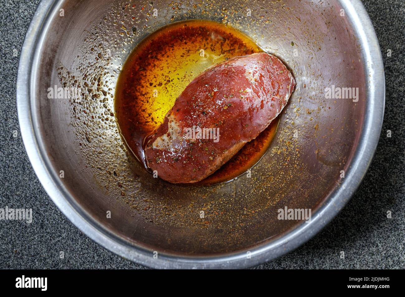 An organic raw duck fillet, being marinated in a metal mixing bowl and ...