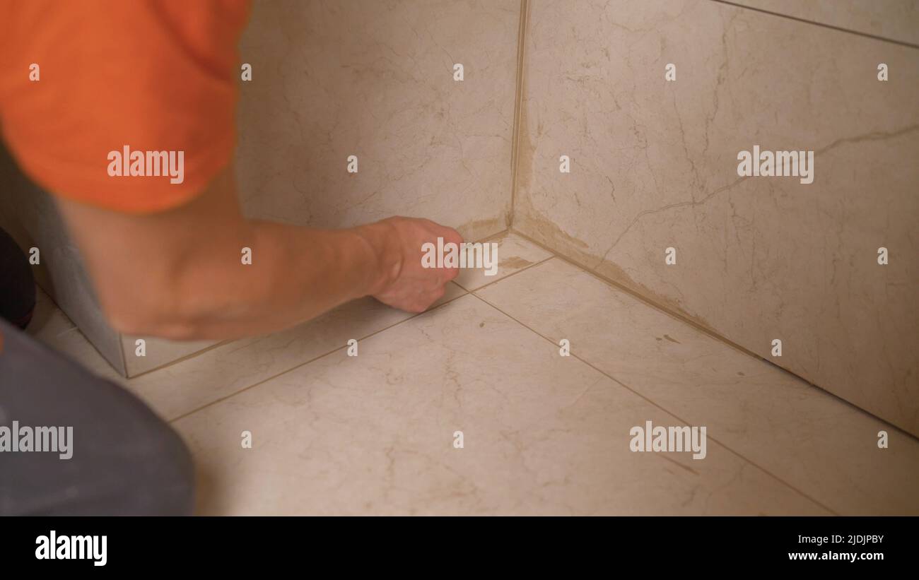 A human hand rubbing the seams of tiles with a spatula. DIY repair ...