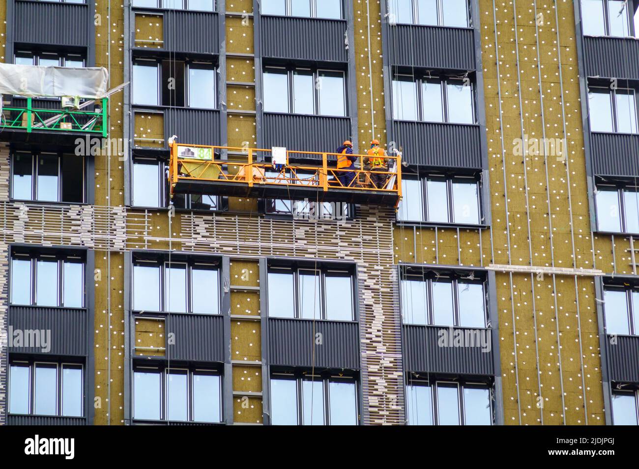 Low angle of contractors in protective uniform standing on cradle ...