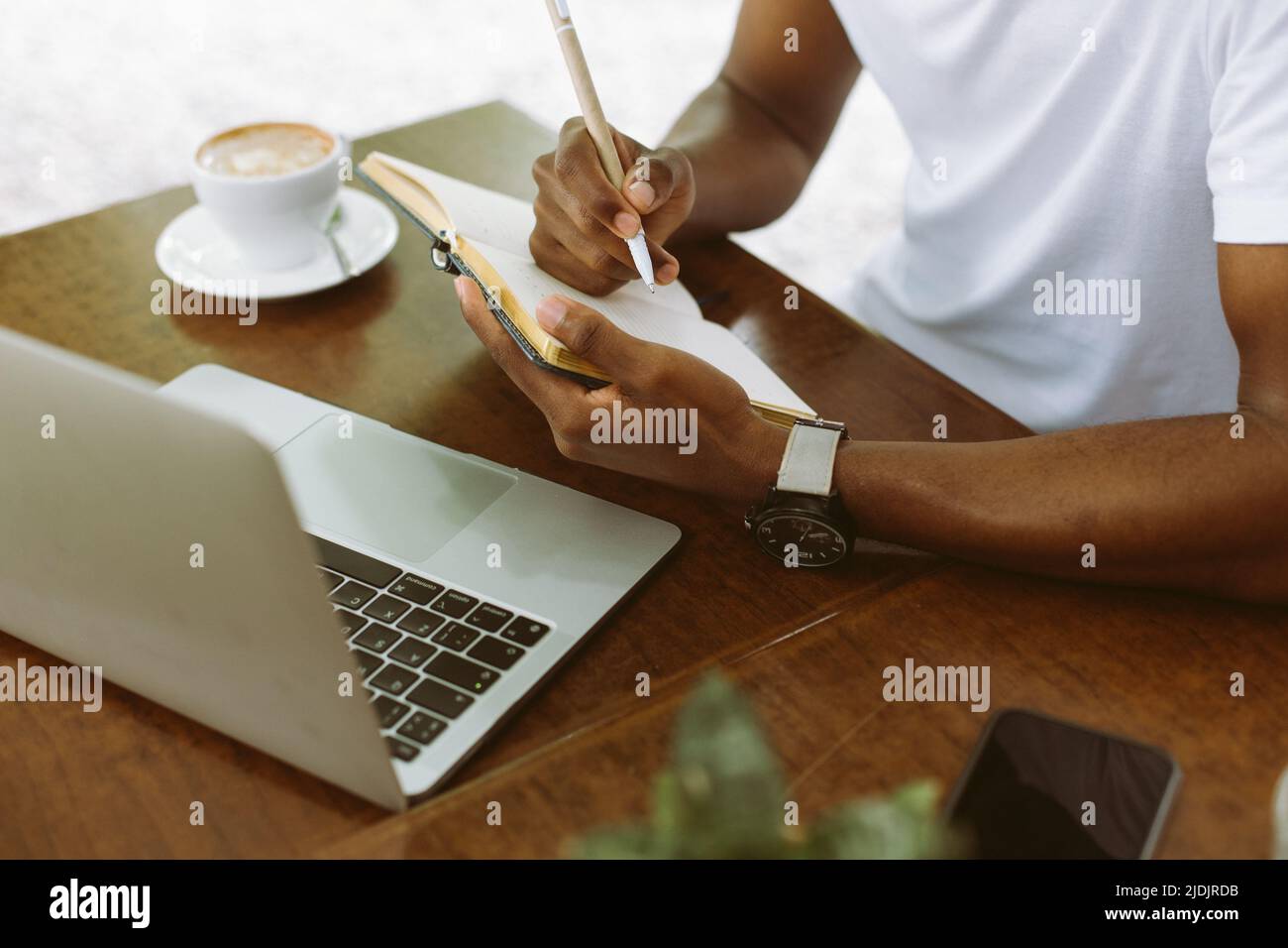 Unrecognizable cropped multicultural man using laptop, taking notes in ...