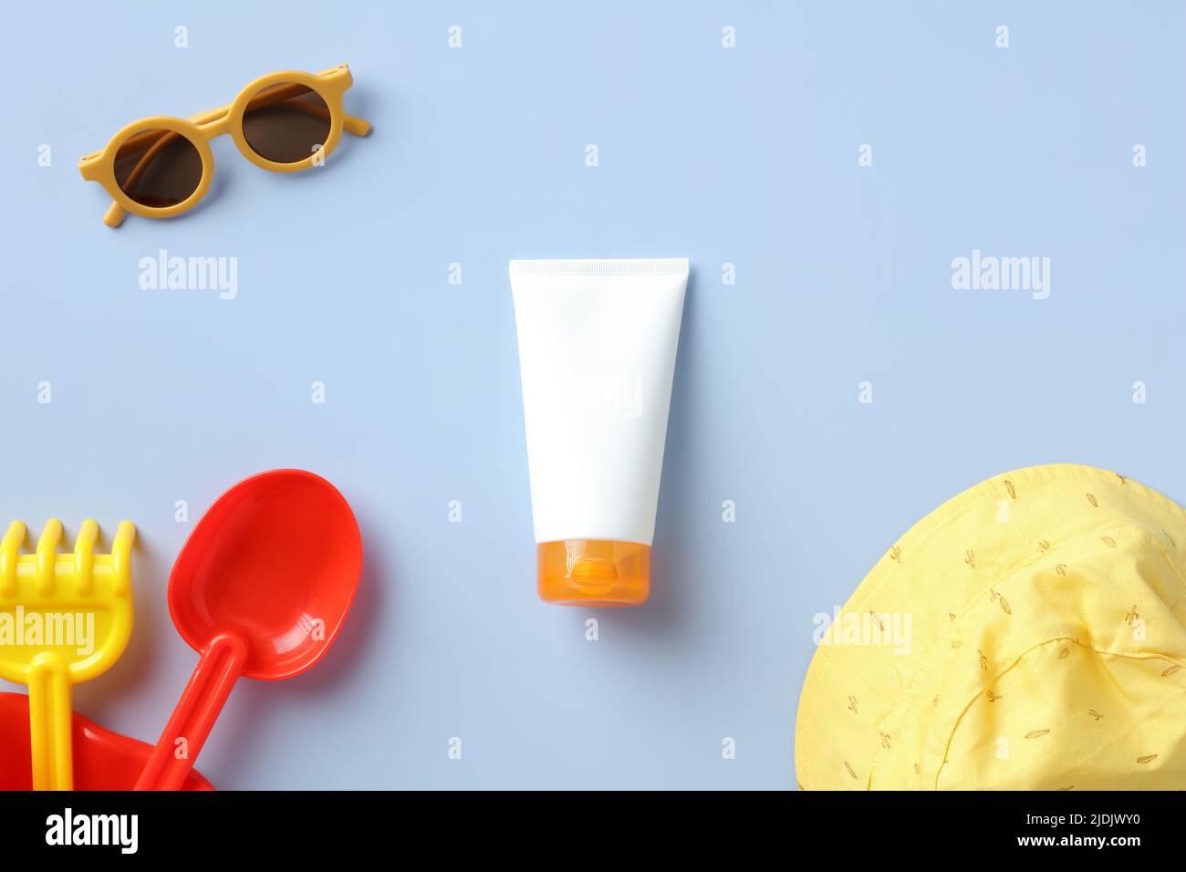 Sunscreen cream tube, sunglasses, panama hat, sand molds on blue table ...