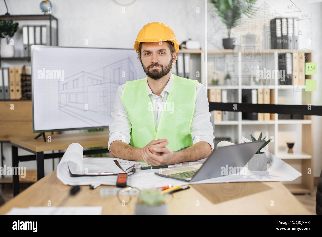 Bearded engineer man in yellow helmet and reflective vest sitting at ...