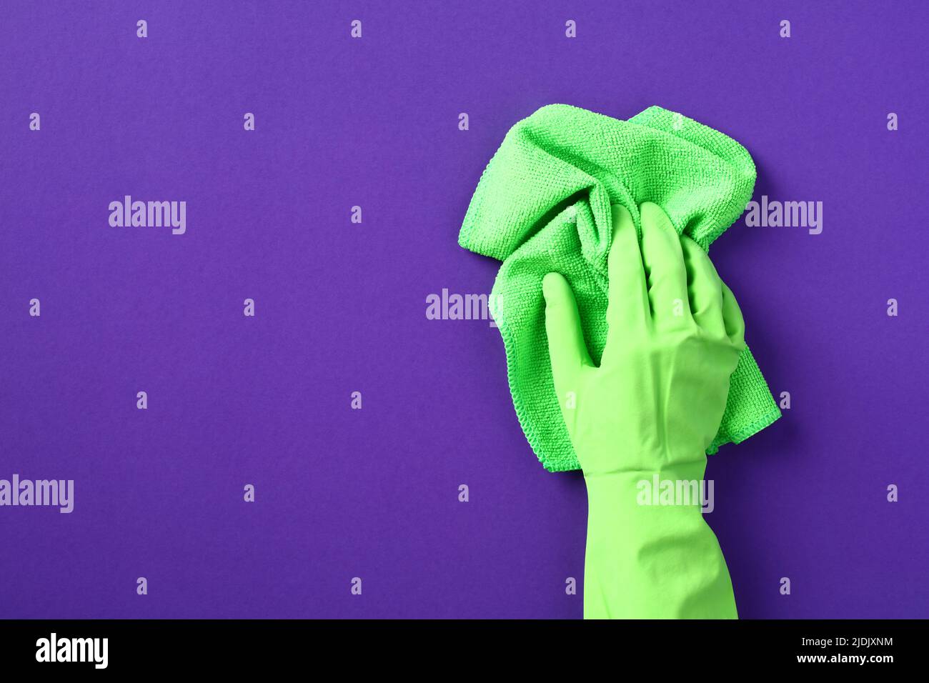 Female hand in green protective glove with green rag over purple ...