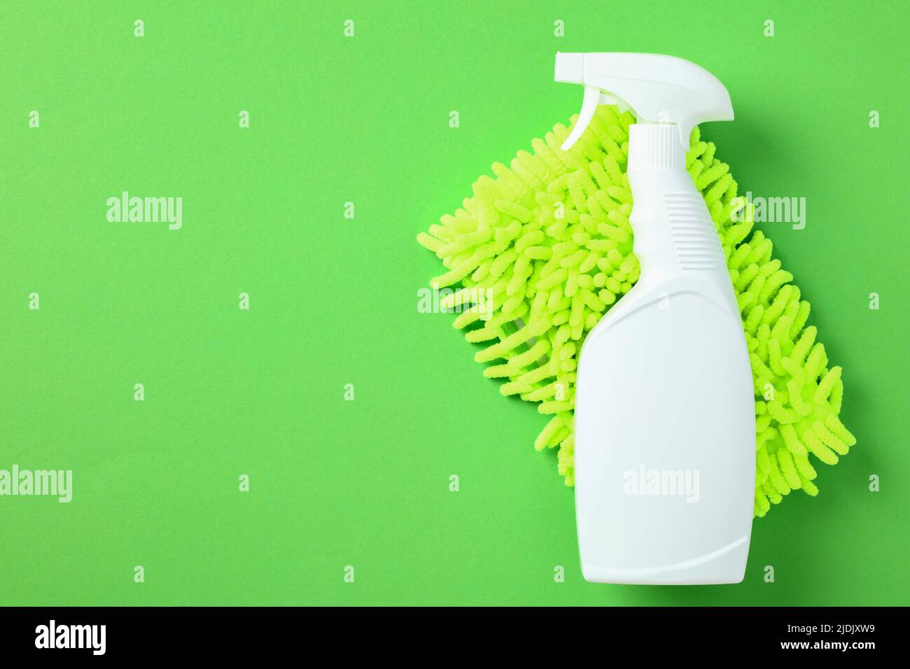 White cleaner spray bottle and rag on green background. Flat lay, top ...
