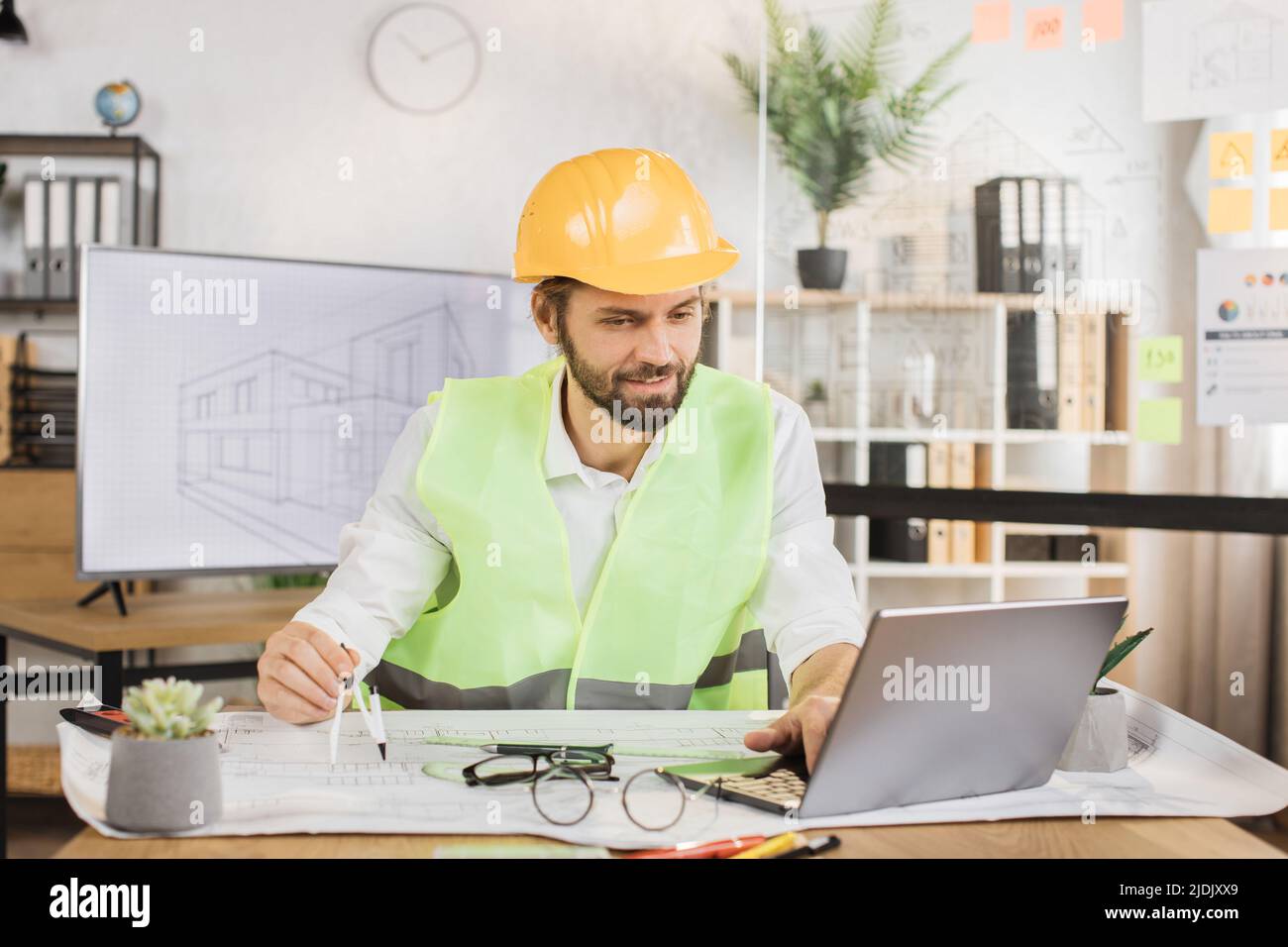 Competent architect male sitting on desk indoors with digital laptop ...