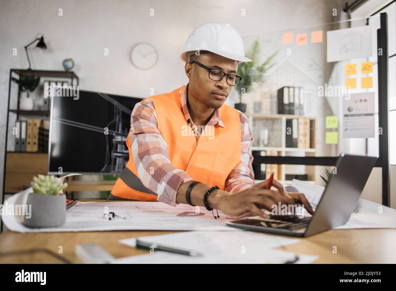 Young architect african male in helmet and uniform sitting at table ...
