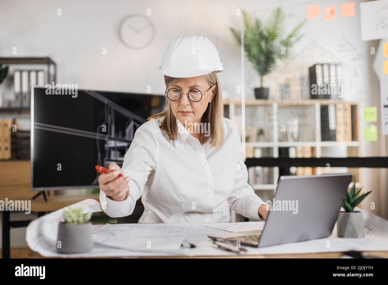 Mature architect woman or female builder holding pen while writing and ...