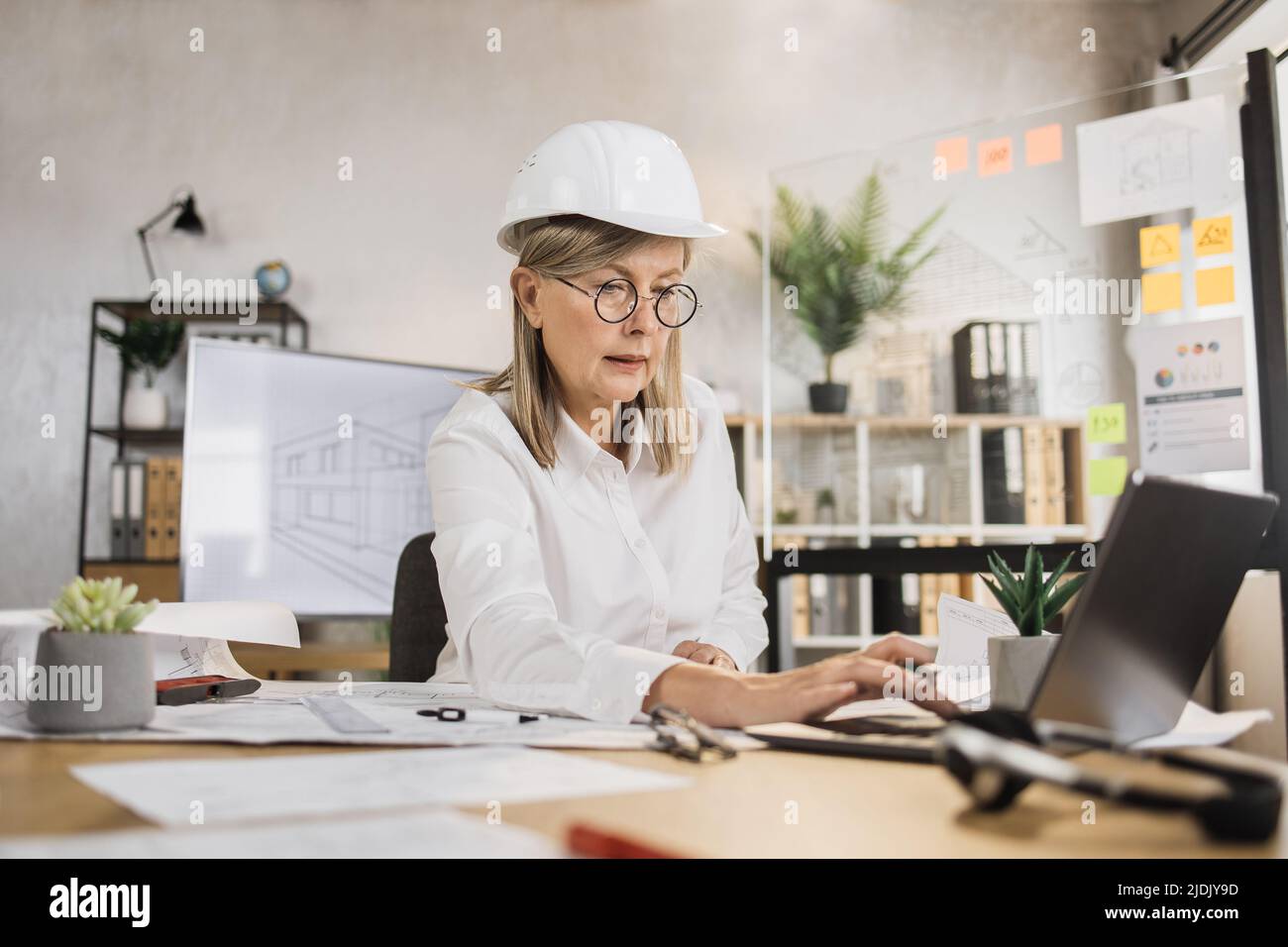 Portrait of professional caucasian mature female architect using laptop ...