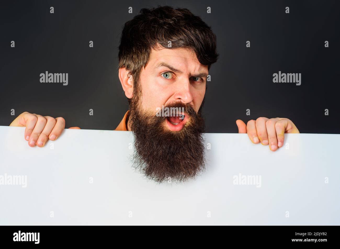 Confused bearded man with advertising banner. Handsome guy shows empty ...