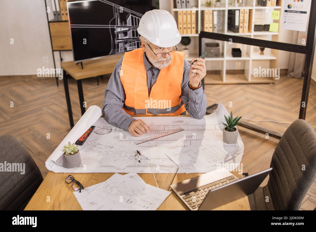 Competent architect senior male sitting on desk indoors with digital ...