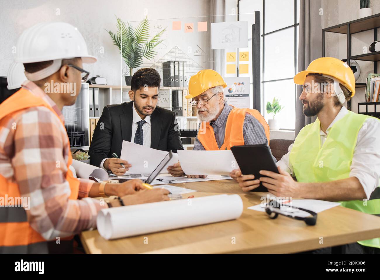 Multiracial men builders in formal outfit and helmets sitting at table ...