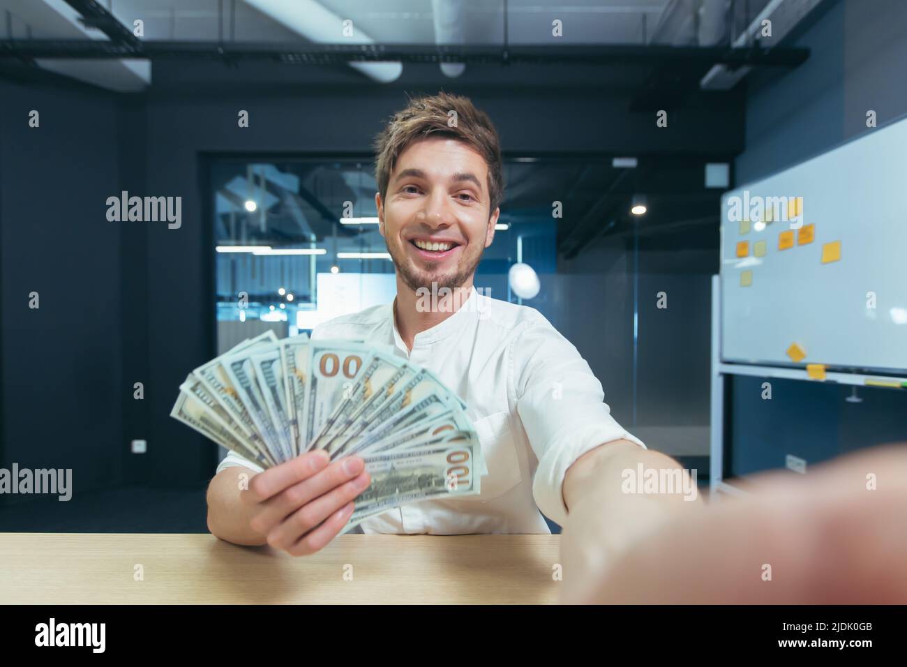 Happy young man received a salary. He holds money in his hands, points ...