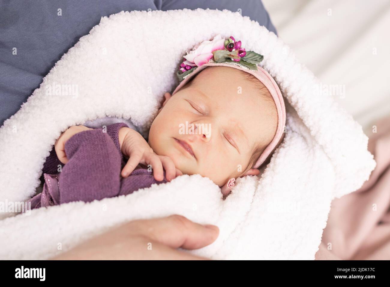 Sleeping newborn baby girl wrapped in a white fluffy blanket in the ...