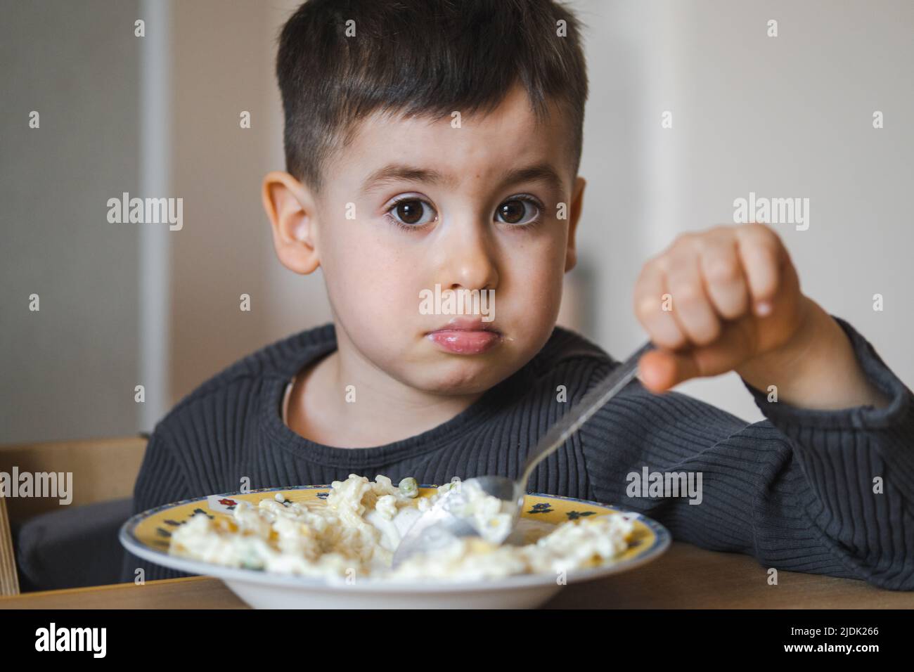 A six-year-old boy sitting at a table eating oatmeal in the morning ...