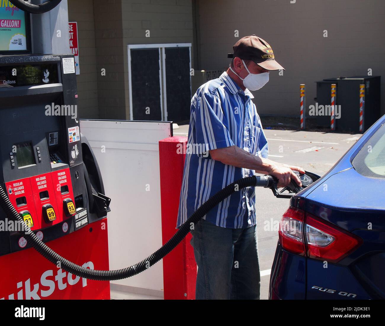 senior wears covid mask as he pumps gas into his hybrid car at a ...