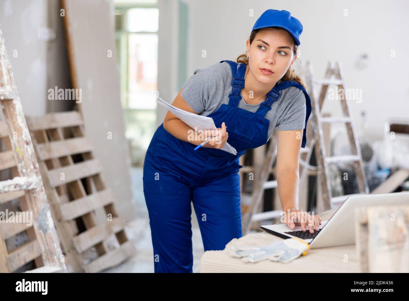 Portrait of a female builder who checks the work done using laptop ...