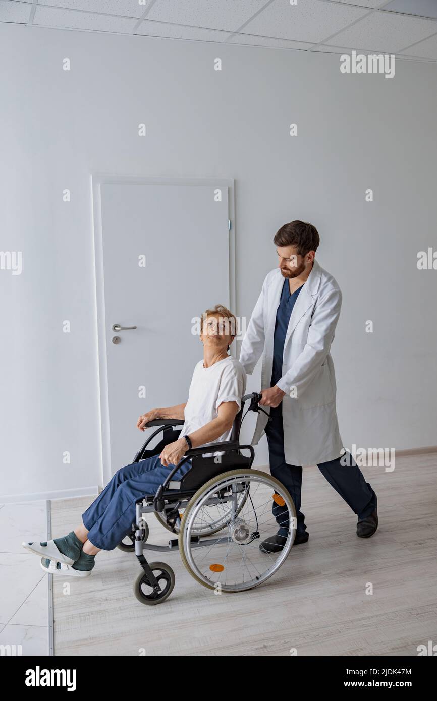Professional male doctor carrying female patient on wheelchair in ...
