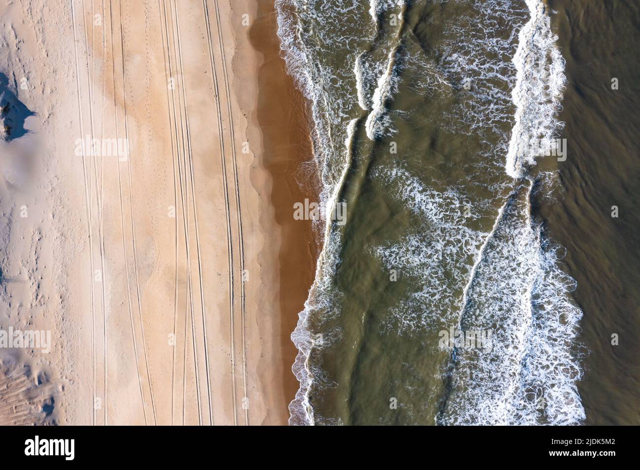 Aerial view of waves breaking with tire tracks in the sand Stock Photo ...