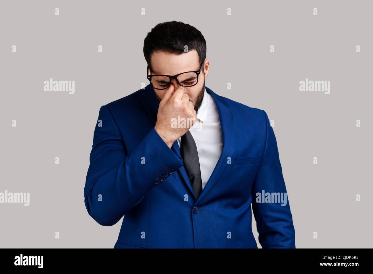 Bearded businessman standing with head down, rubbing eyes, putting off ...