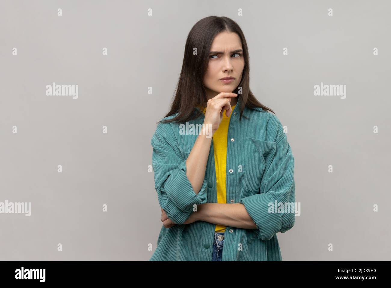 Confused puzzled woman standing holding her chin and looking aside ...