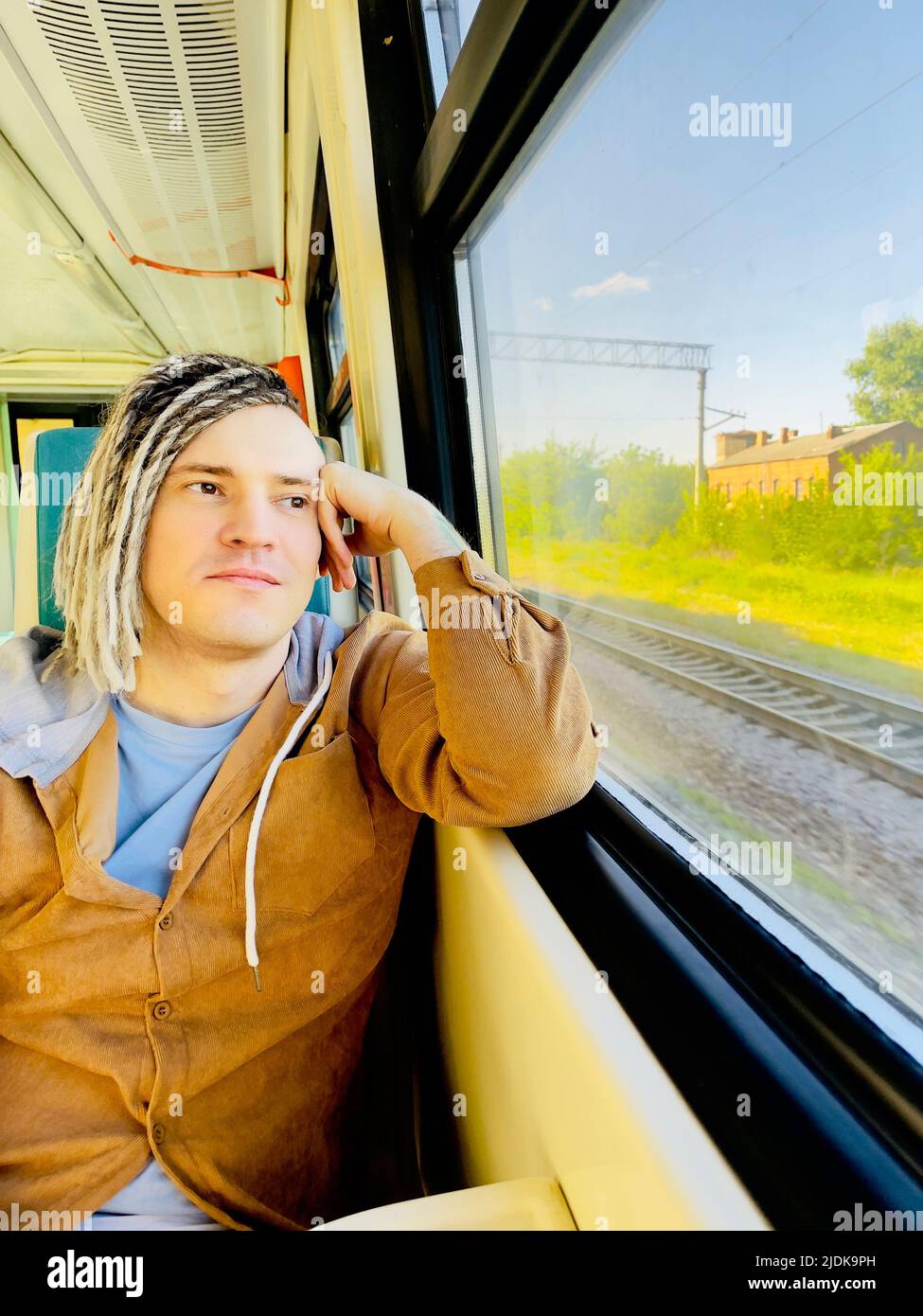 Young relaxed man riding on train. Dreamy guy with blonde dreadlocks ...