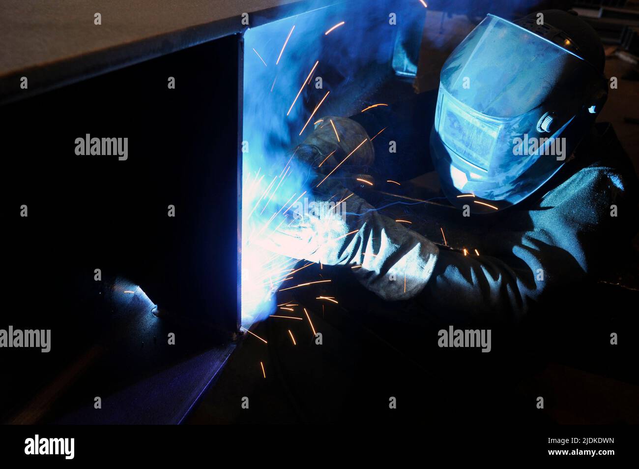 A welder in protective overalls and a welding mask welds metal ...