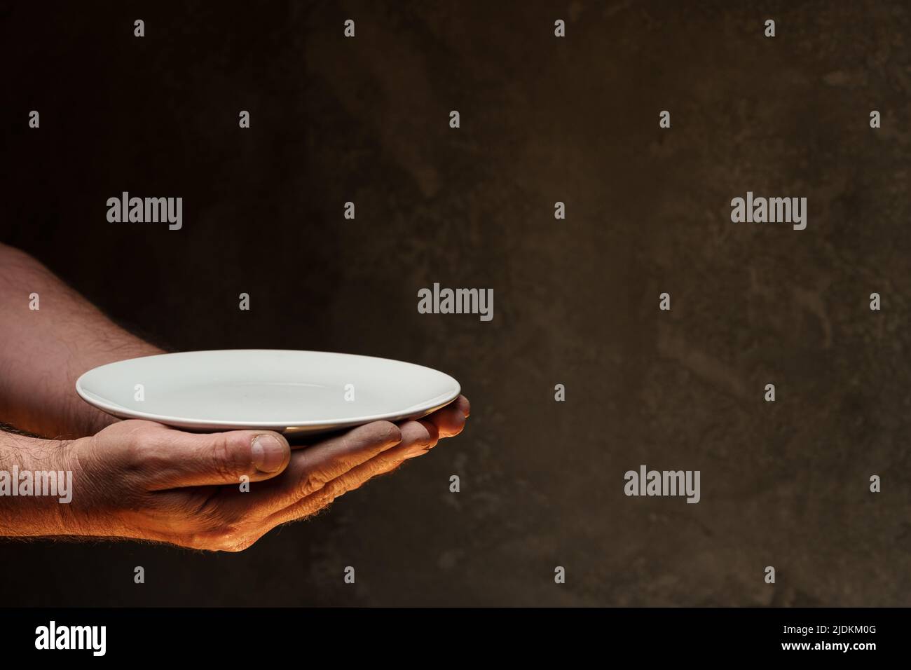 Male hands holding empty plate on dark background, lack of food, hunger ...