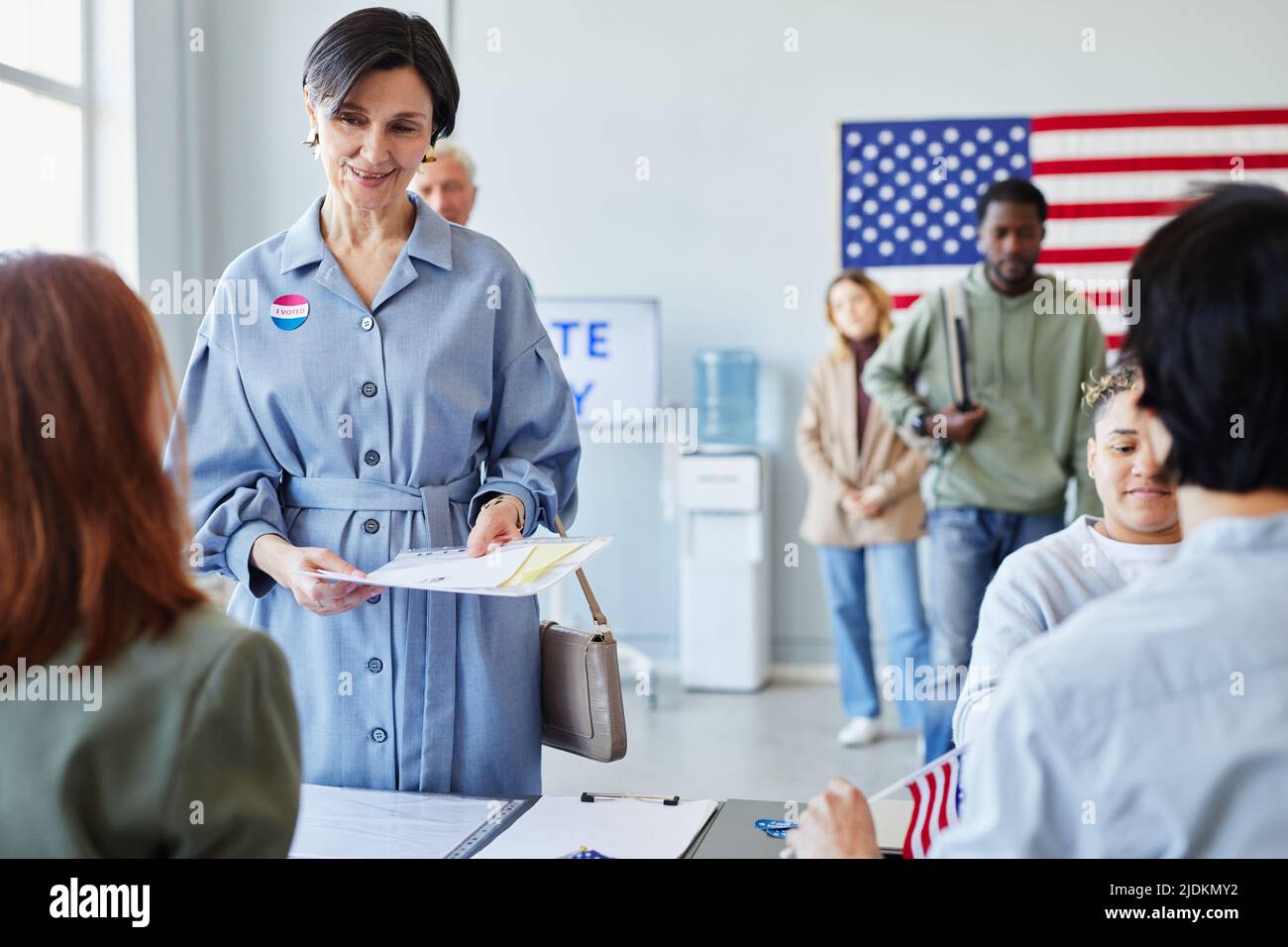 Front view portrait of smiling adult woman receiving ballot at voting ...