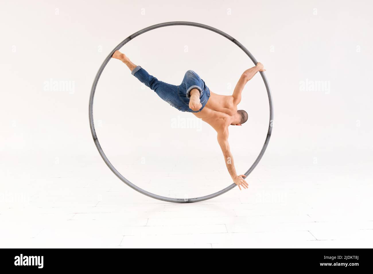 Fit male acrobat performing a one leg handspring on a cyr wheel while ...