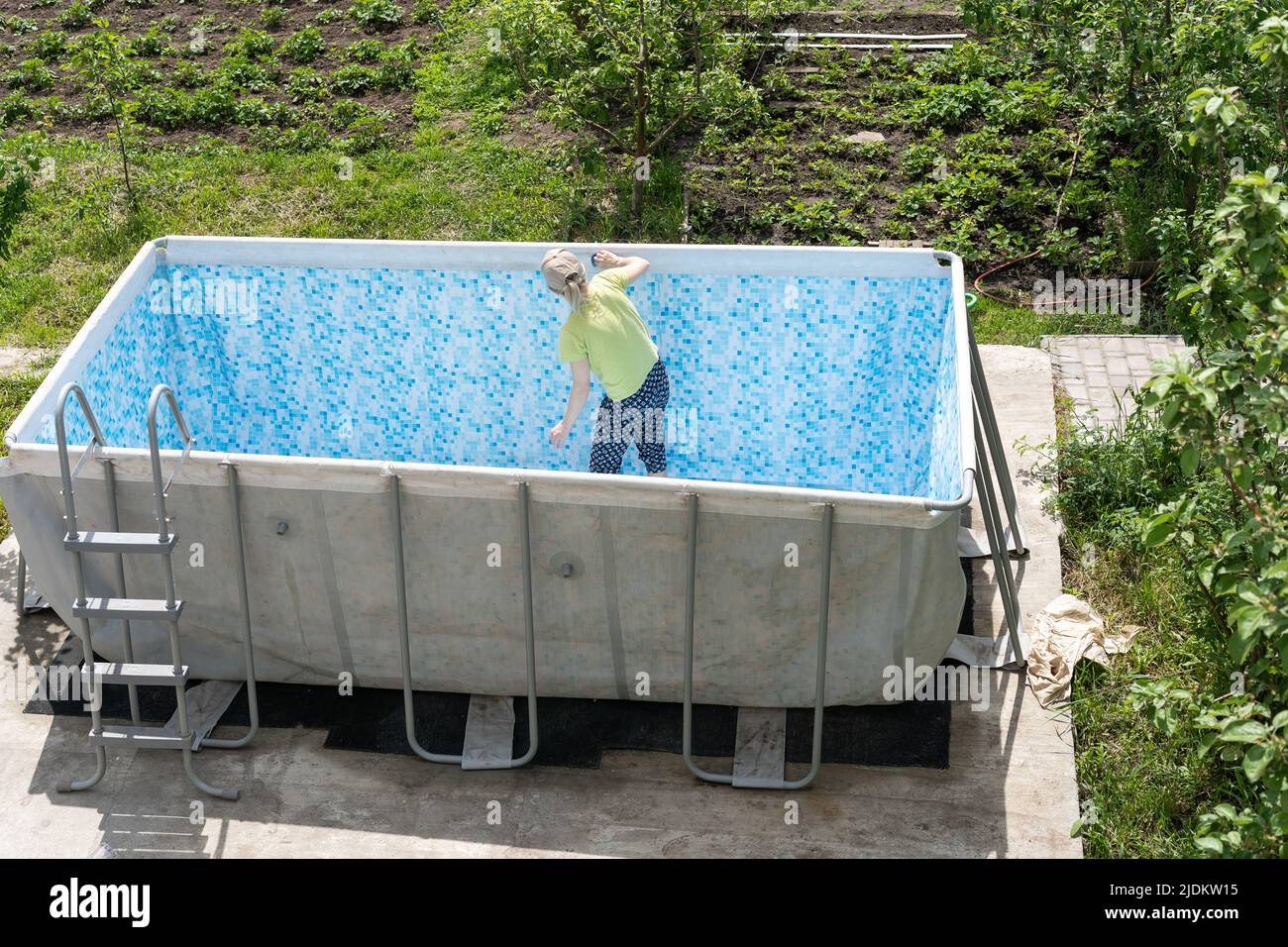 woman cleans the empty pool in the yard against the background of ...