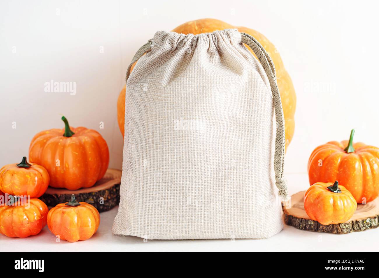 Empty jute beige gift bag and many pupkins on white marble table, fall ...