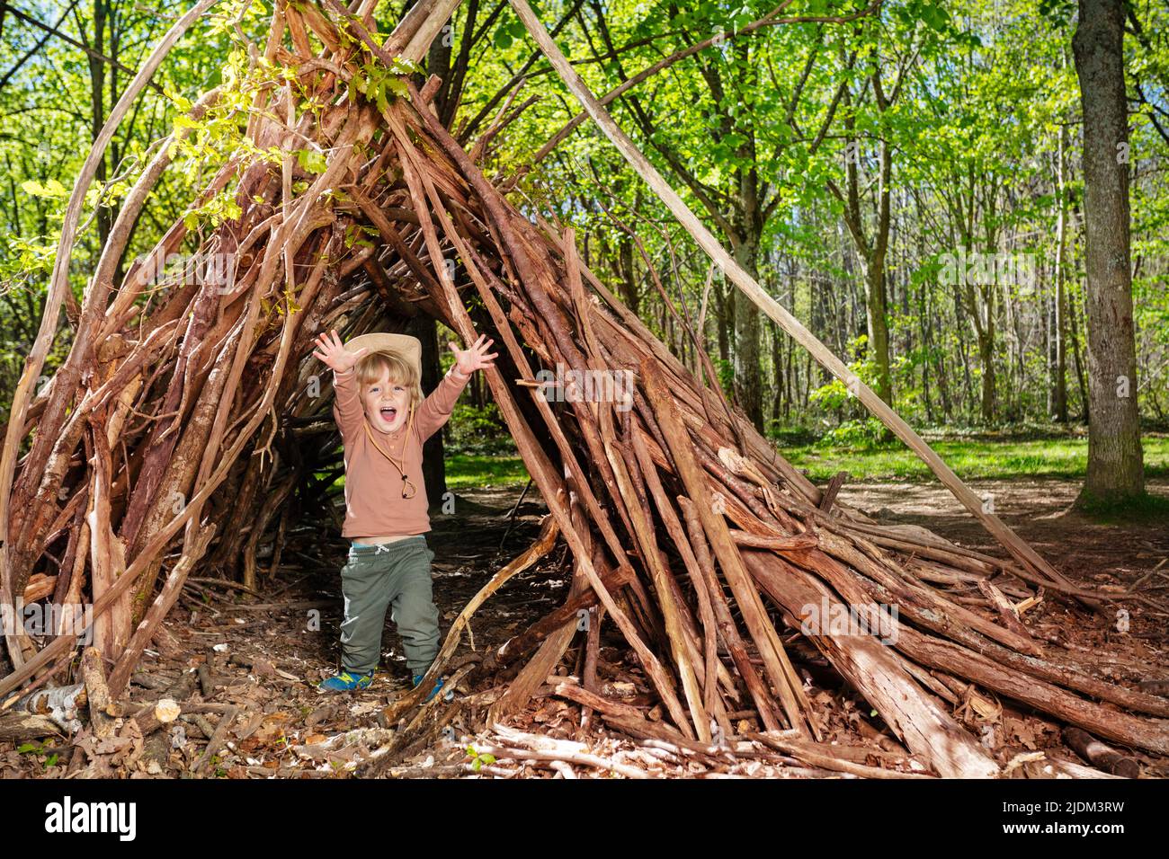 Blond boy play in the hut of branches lifting hands up Stock Photo - Alamy