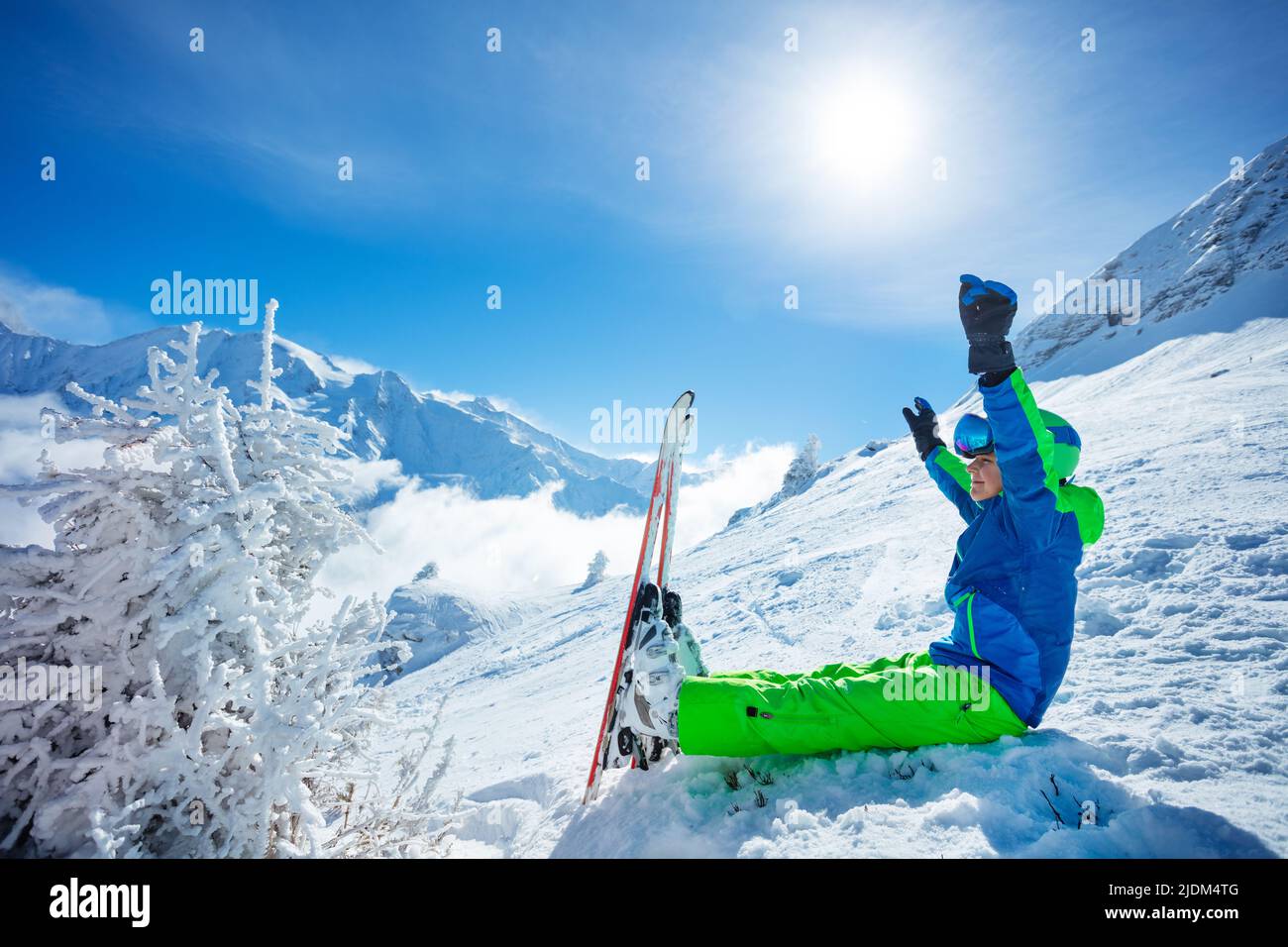 Boy with alpine ski and helmet sit in snow lifting hands Stock Photo ...