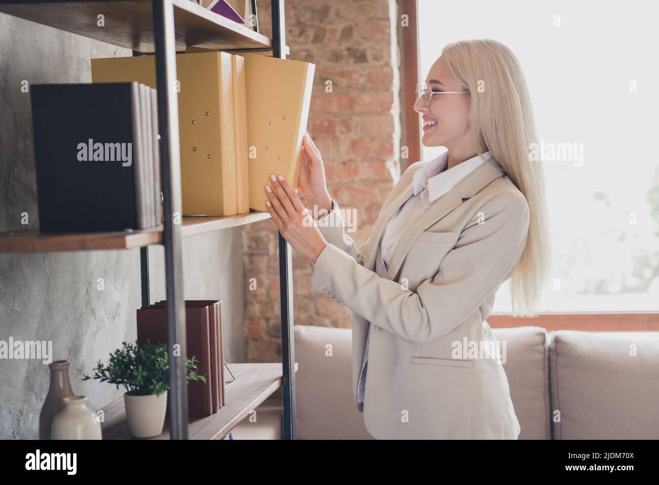 Profile portrait of cheerful charming lady stand bookshelf take ...