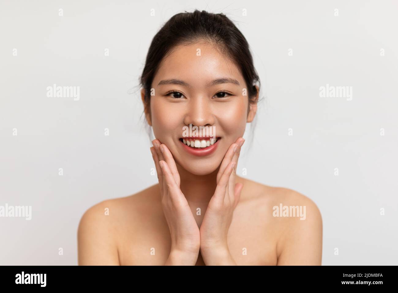 Happy young asian lady touching her cheeks and smiling at camera ...