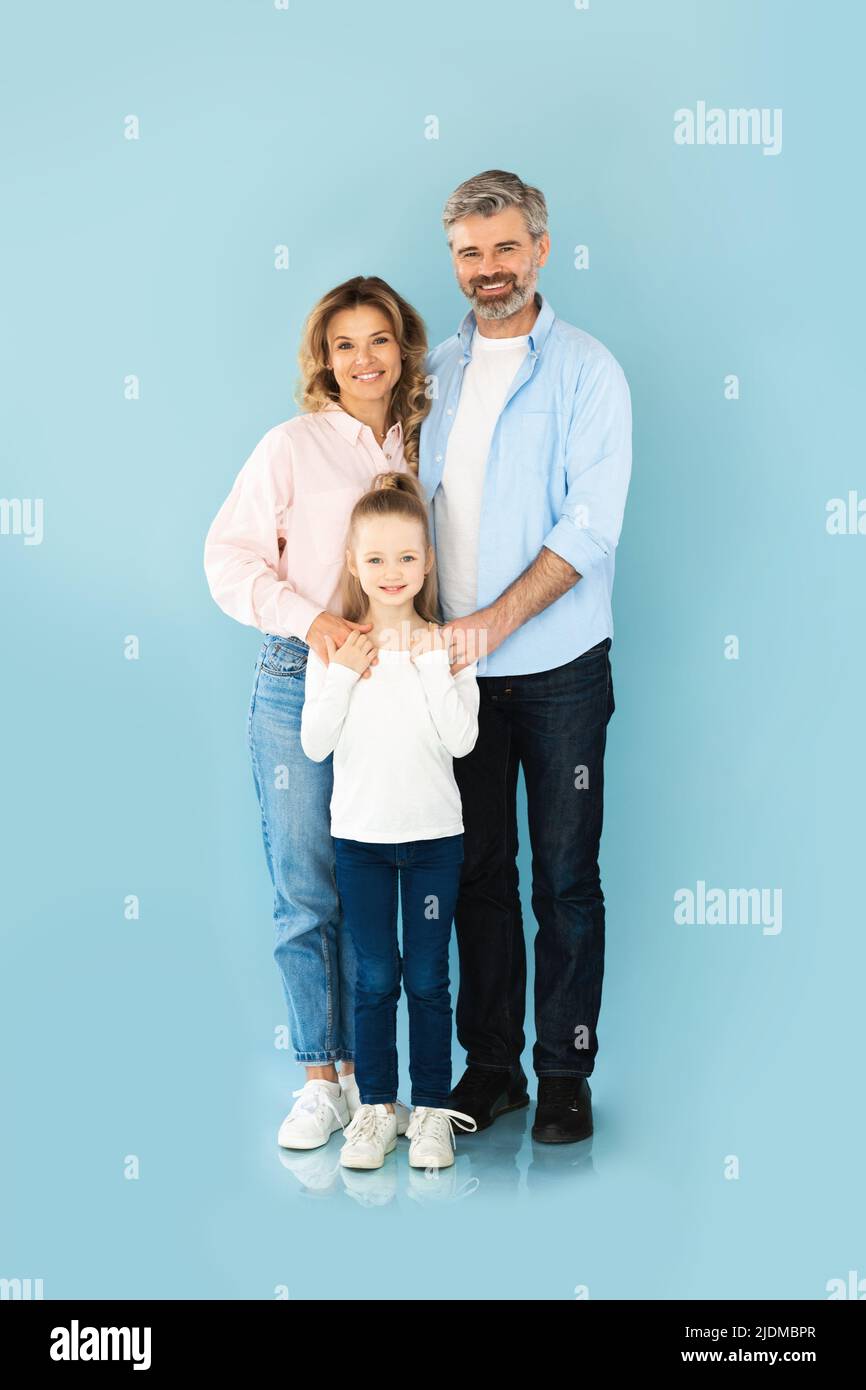 Parents Hugging Their Little Daughter Standing Over Blue Background ...