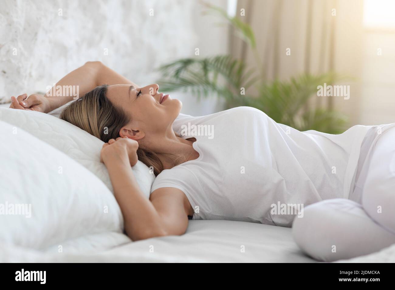 Well-rested blonde woman enjoying happy morning, stretching in bed ...