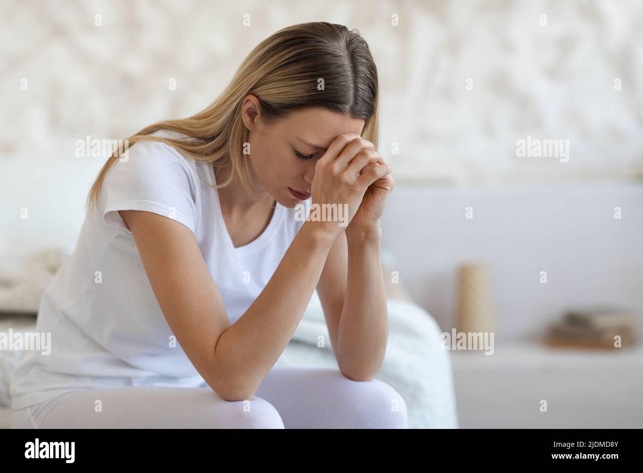 Upset blonde lady sitting on bed at home, crying Stock Photo - Alamy