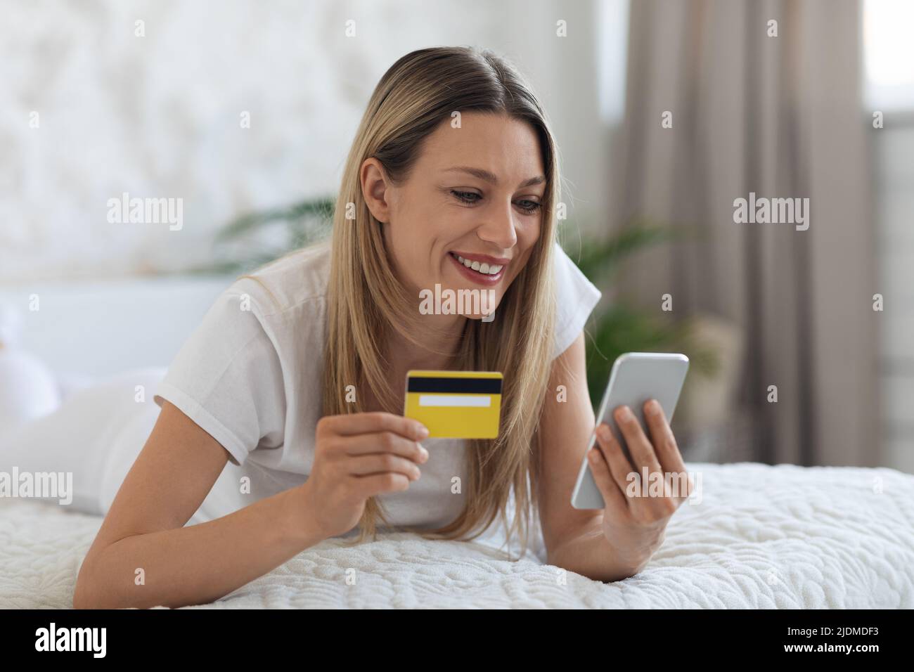Positive woman laying in bed with smartphone and credit card Stock ...