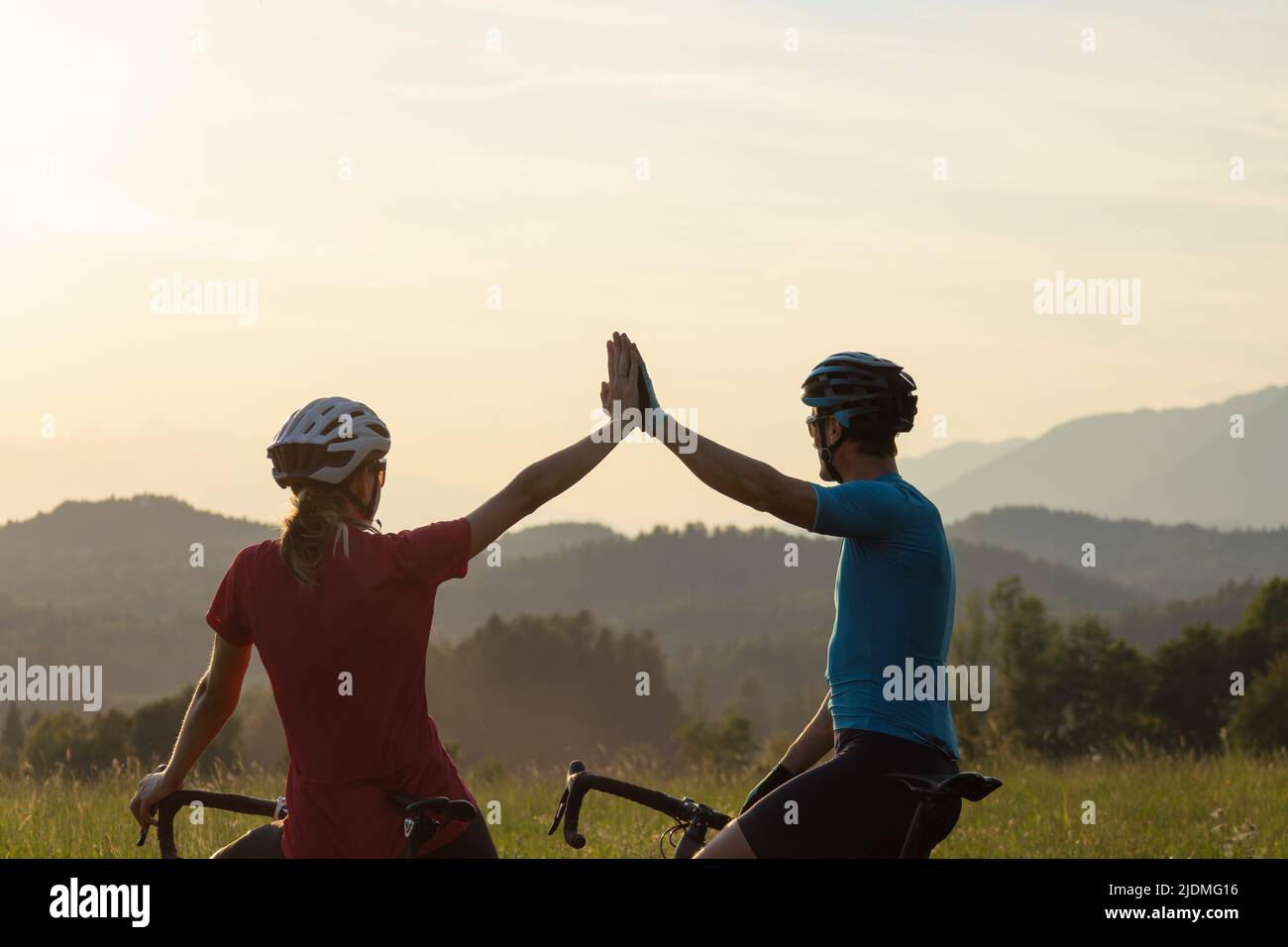 Two road cyclists silhouettes celebrating a ride finish with a high ...