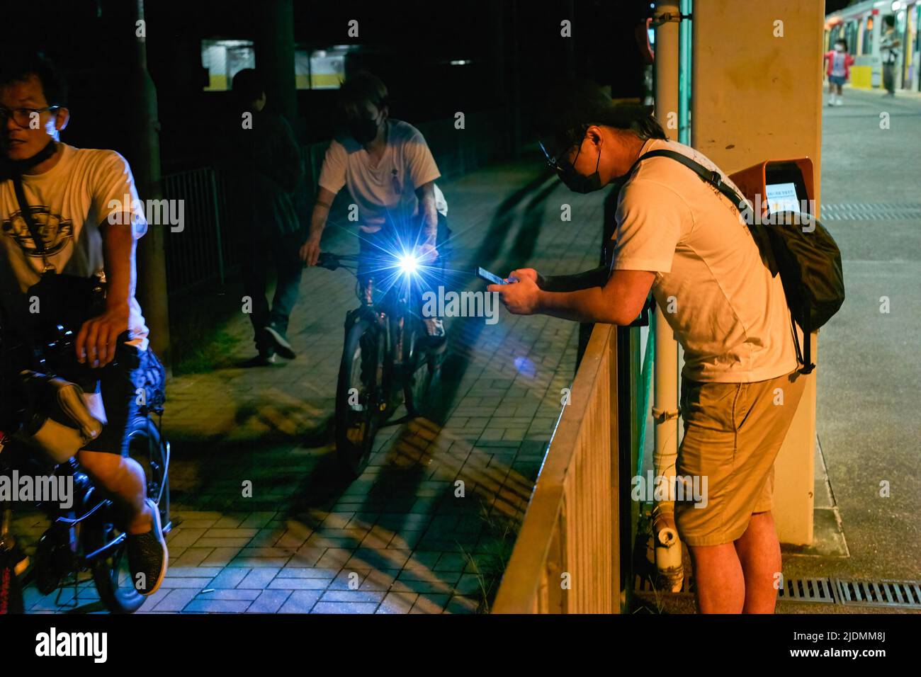 A man looks at his smartphone as two men cycle past the light train ...