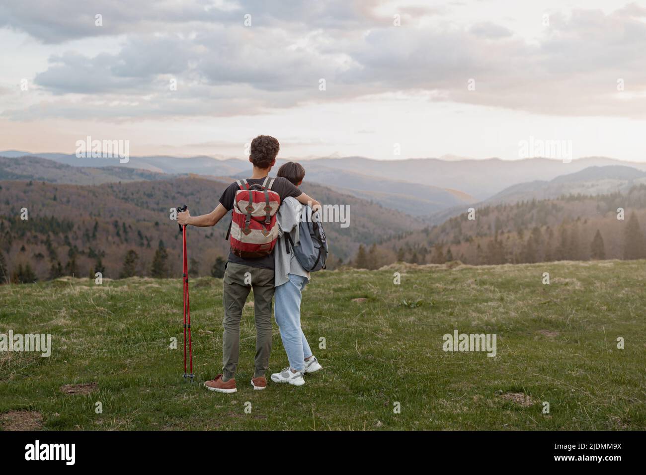 Rear of couple in love and hugs standing on mountain peak with walking ...
