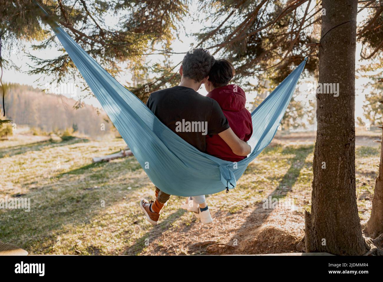 Rear of woman and man sitting in hammock and hugging while having rest ...