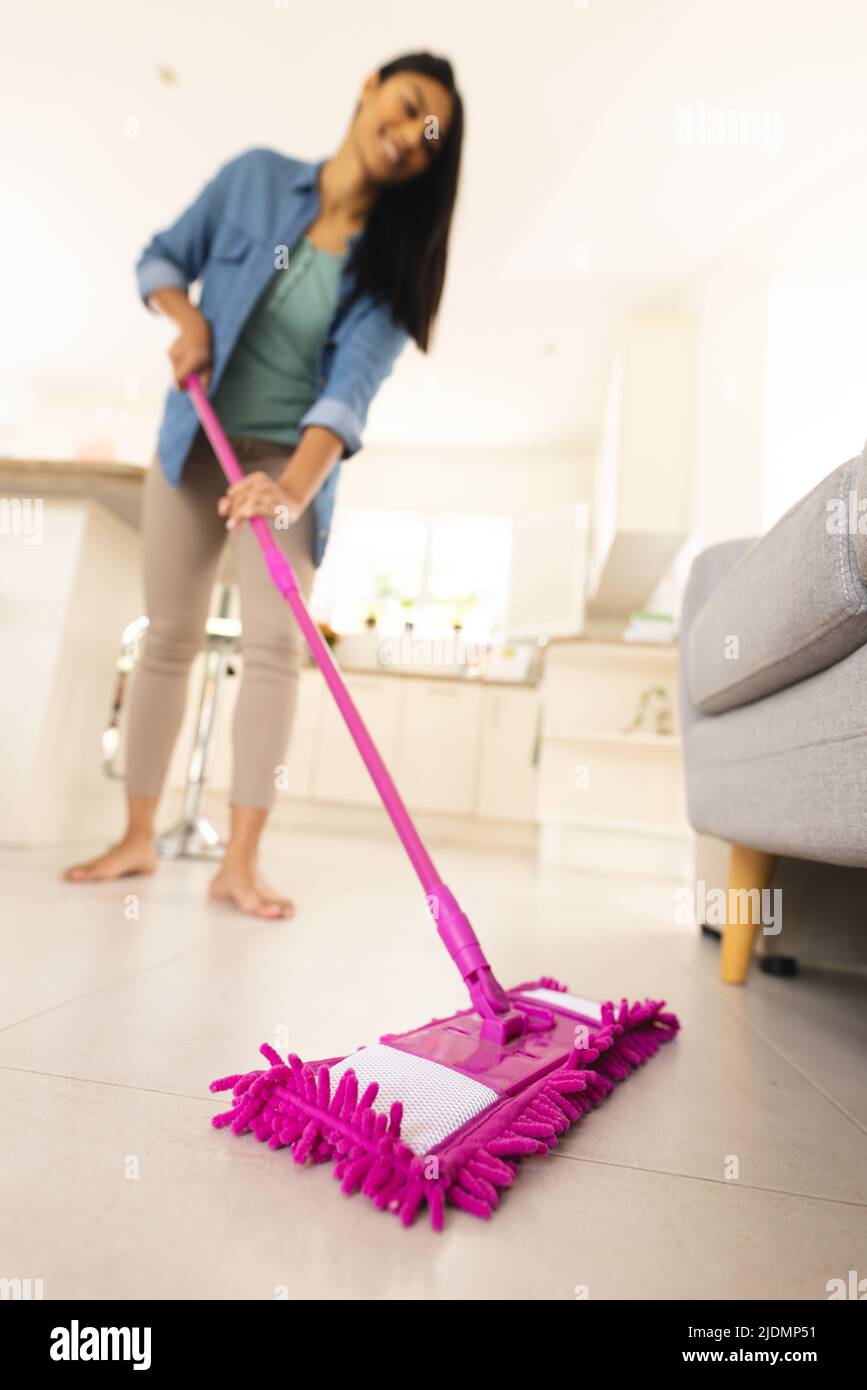 Biracial young woman cleaning floor in living room with pink mop at ...