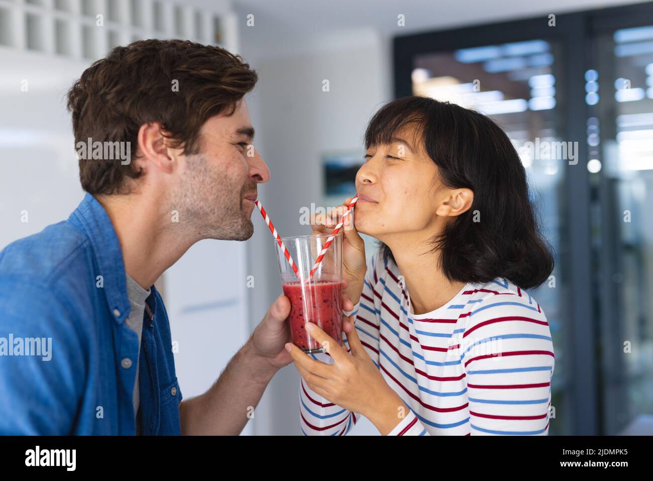 Happy multiracial young couple drinking fruits smoothie through straw ...