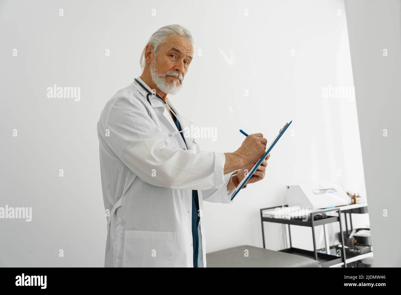 Professional doctor taking notes on clipboard and looking camera in ...