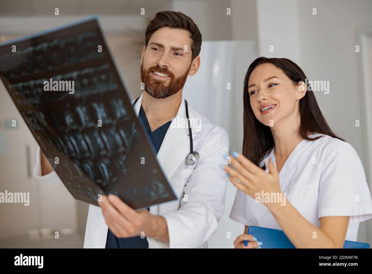 Two of smiling doctors in uniform look and discuss an X Ray or MRI scan ...