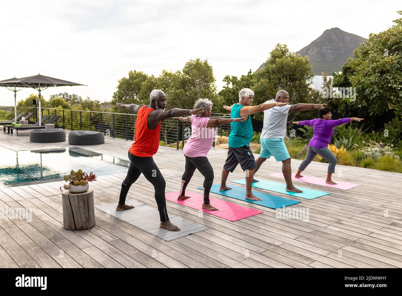Multiracial senior friends practicing warrior 2 pose on mats in yard ...