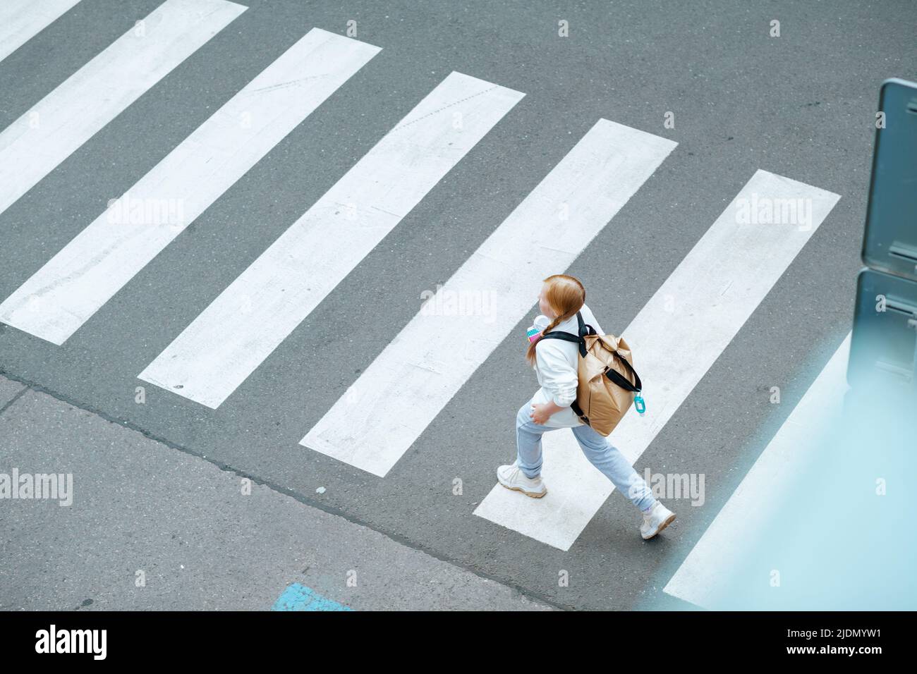 Upper view of modern girl in white sweatshirt with backpack crossing ...